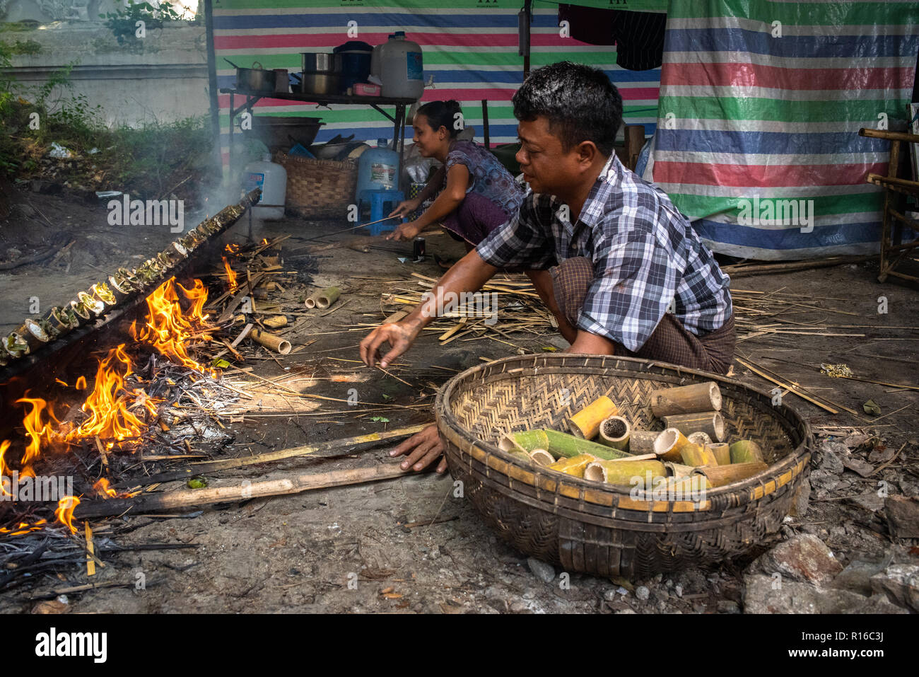 A man and a woman tending to the fires used to cook Bamboo-tube Sticky ...