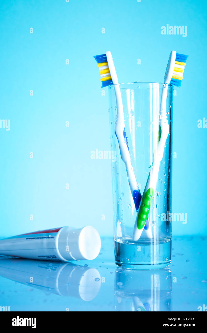 Toothbrushes in a glass beside a tube of toothpaste on a table with ...