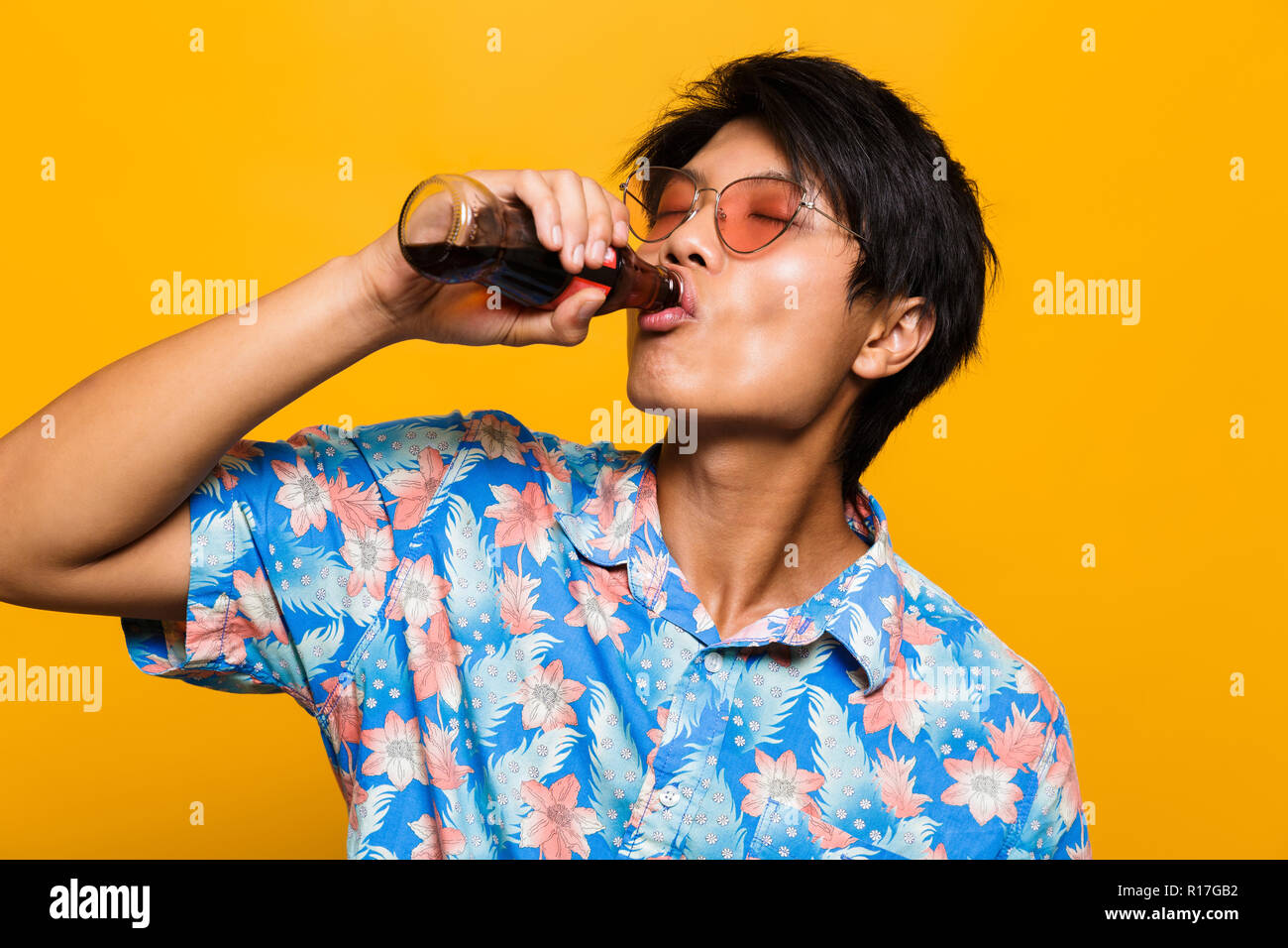 Portrait of a happy asian man isolated over yellow background, drinking ...