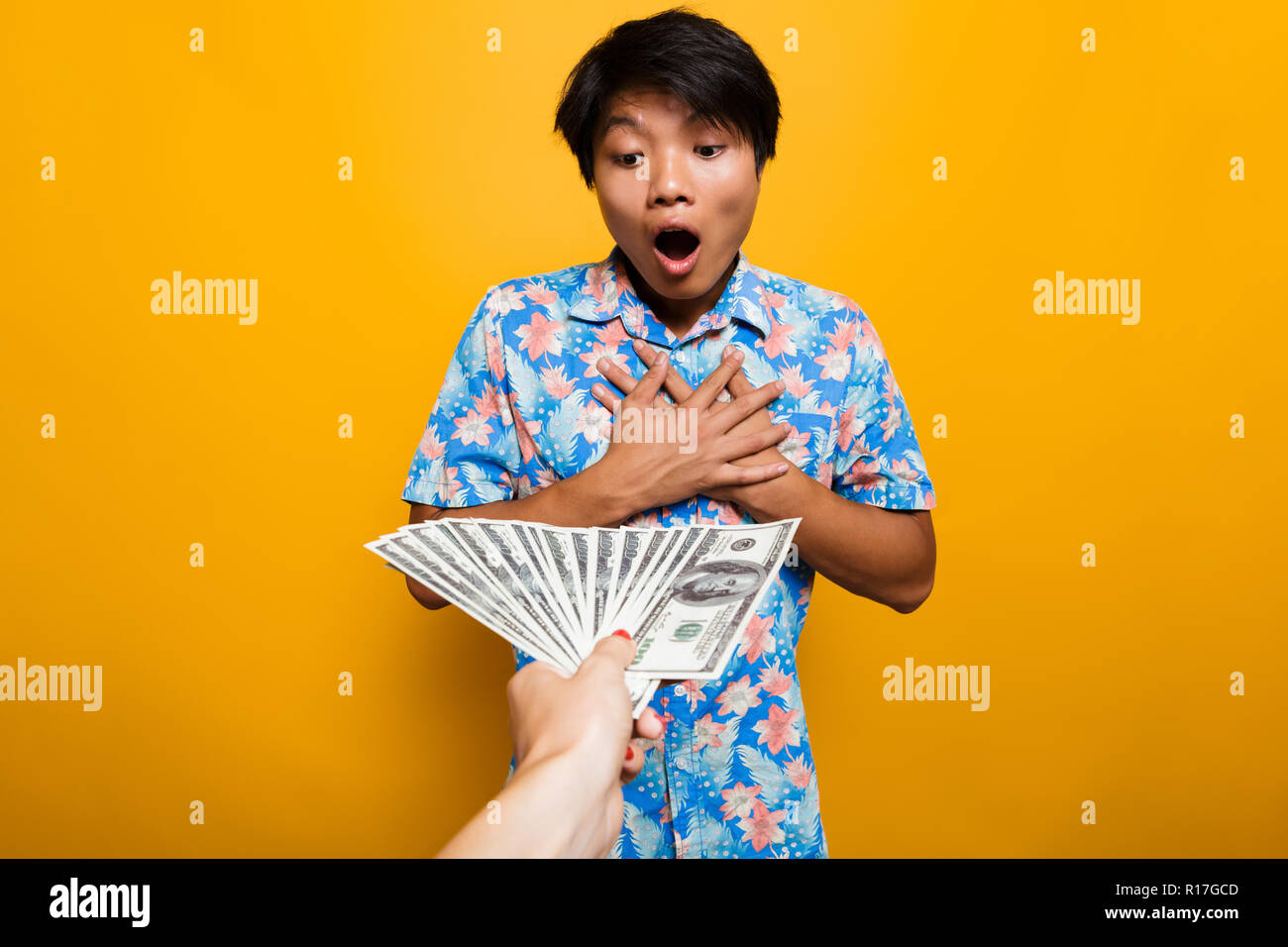 Amazed asian man receiving money banknotes isolated over yellow ...
