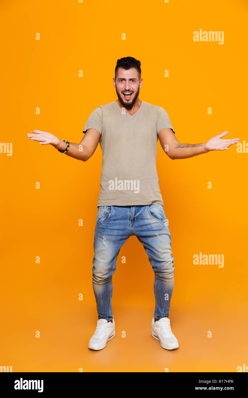 Full length portrait of a confused young casual man standing isolated ...