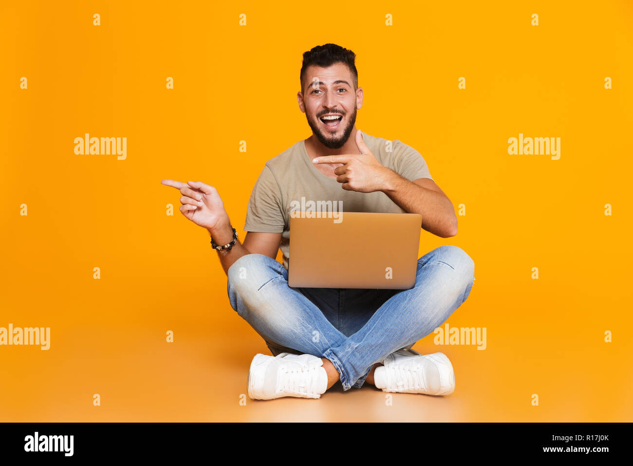 Portrait of a happy young casual man sitting isolated over orange ...