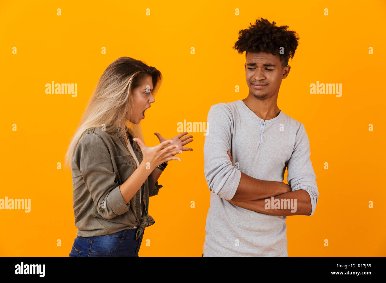 Portrait of an angry multiethnic couple standing isolated over yellow ...