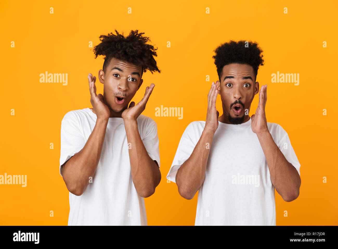 Two shocked male african friends in t-shirts standing isolated over ...