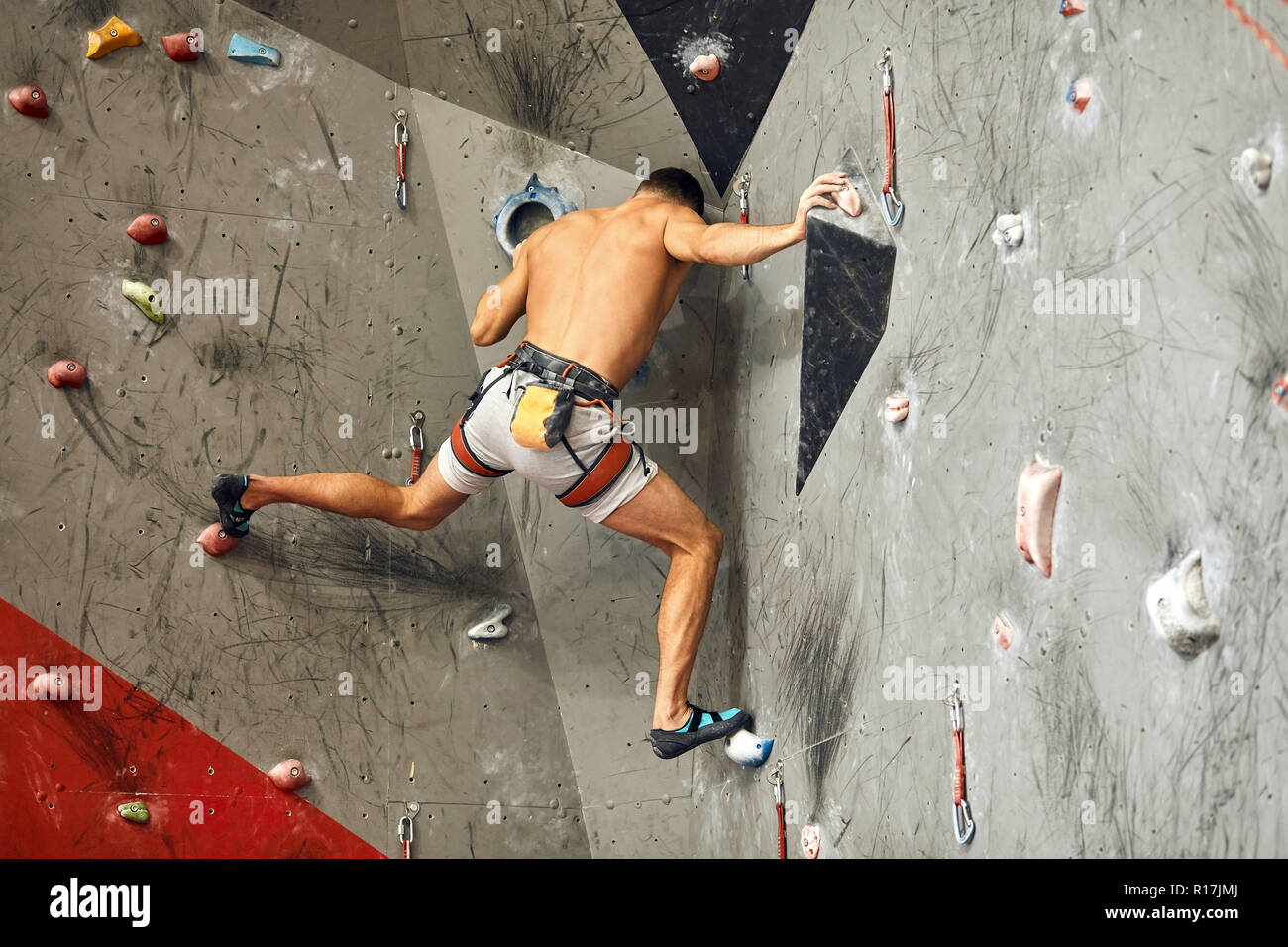 Male climber exercising in gym, climbing up on artificial wall with ...