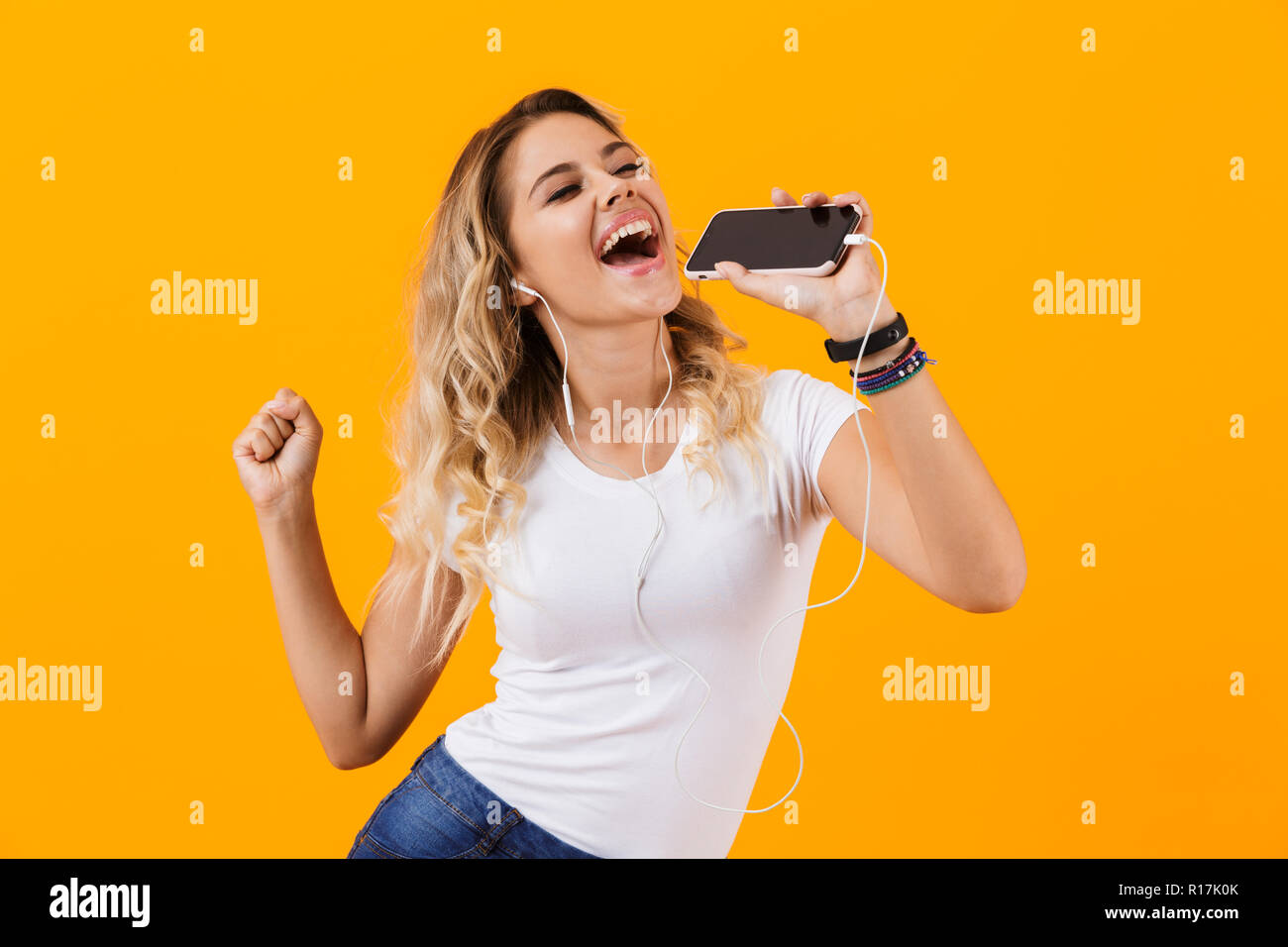 Image of beautiful woman wearing earphones singing while holding cell ...