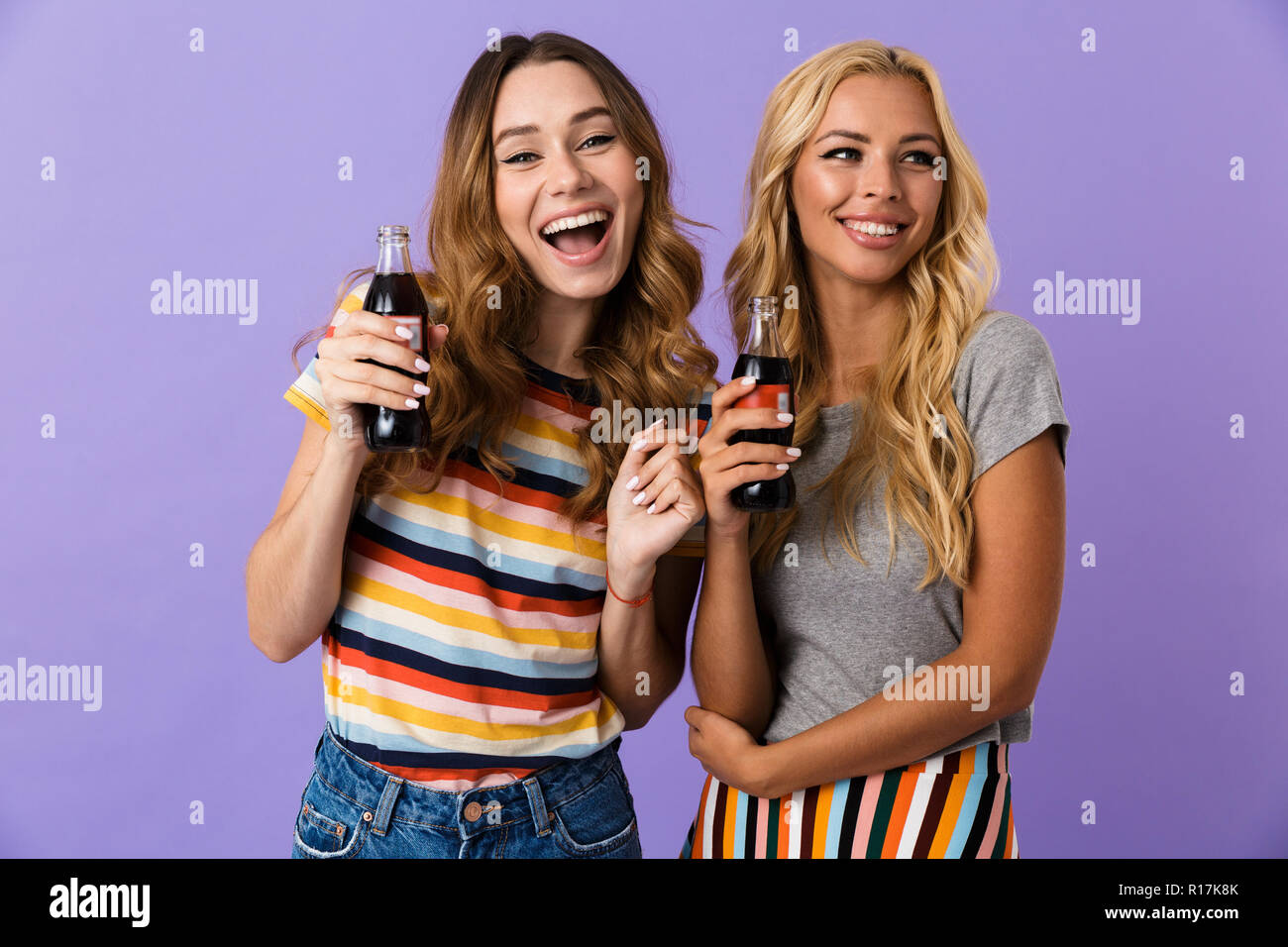 Two pretty cheerful young girls friends standing isolated over violet ...