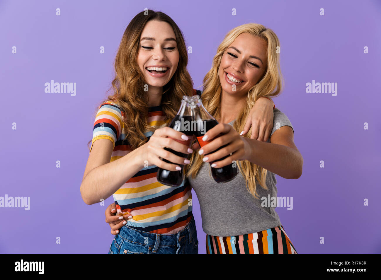 Two pretty cheerful young girls friends standing isolated over violet ...