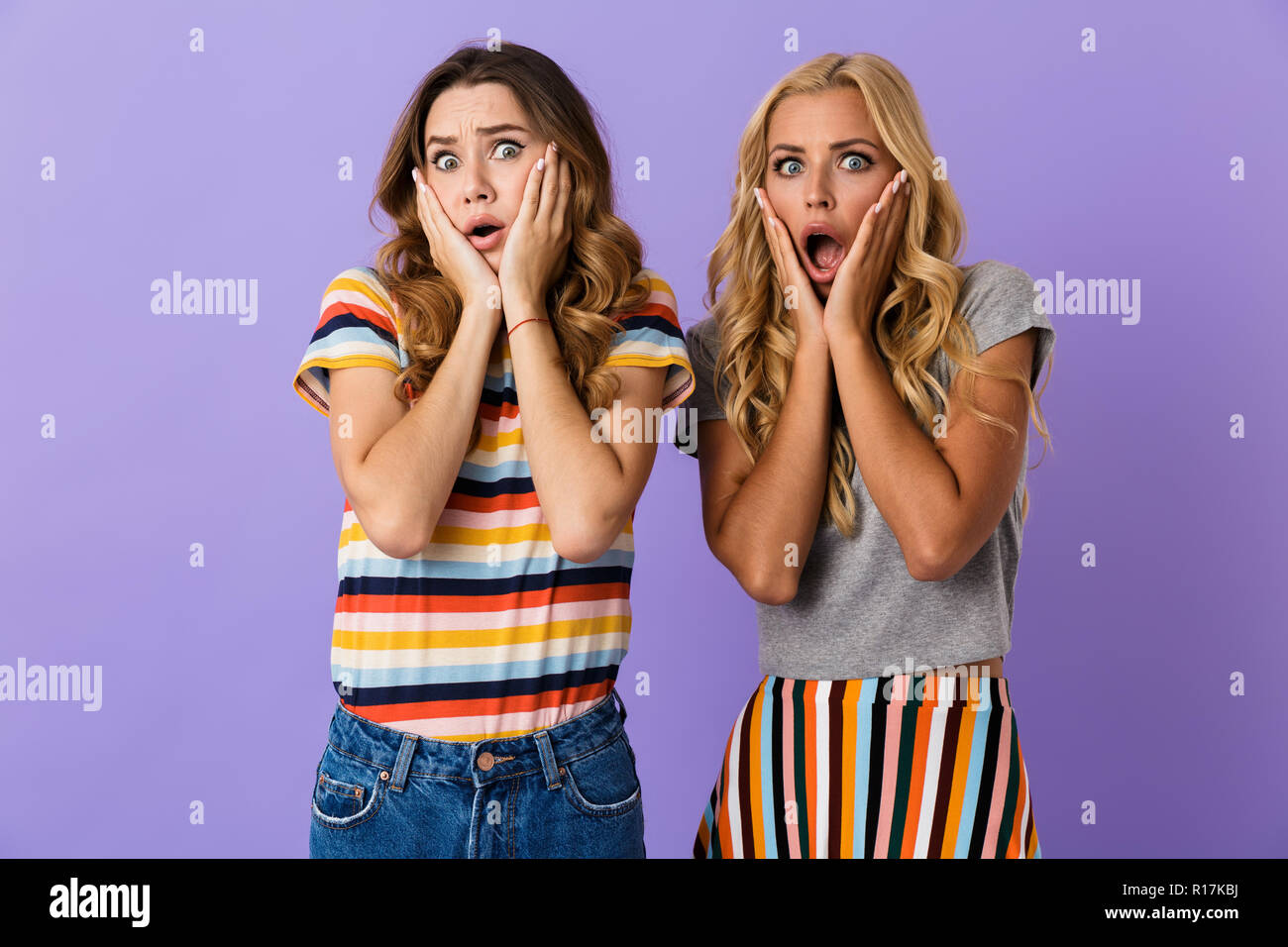 Two pretty scared young girls friends standing isolated over violet ...