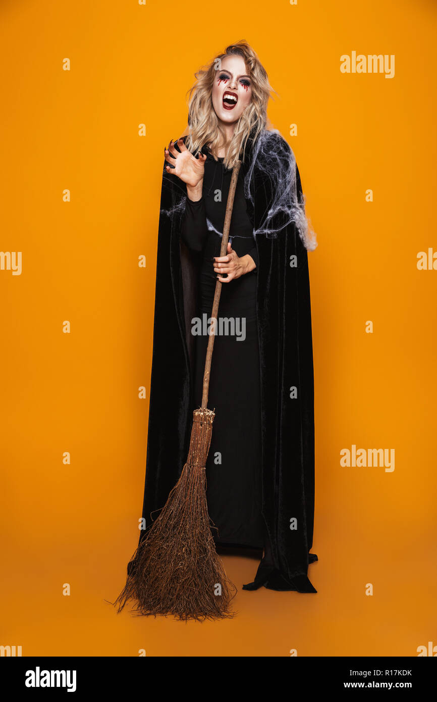 Angry woman witch with scary make-up looking camera and holding broom ...
