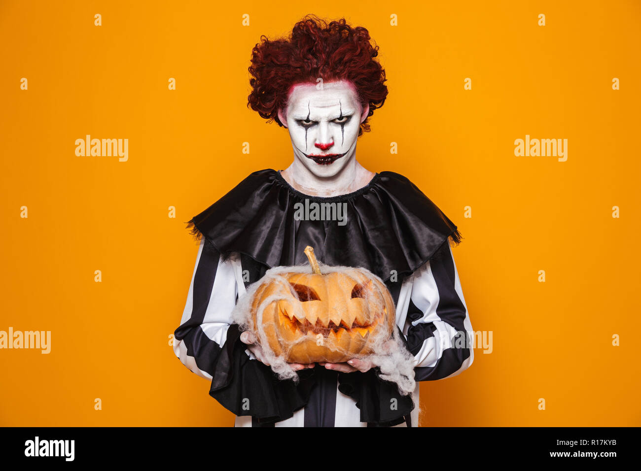 Angry man dressed in scary clown Halloween costume holding curved ...