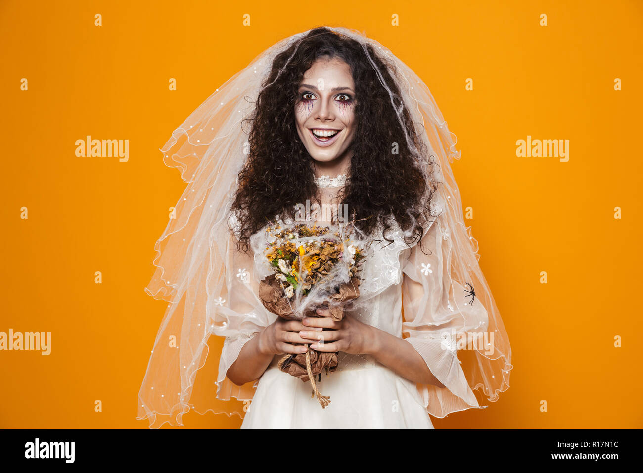 Smiling dead bride in wedding dress and veil holding flowers and ...