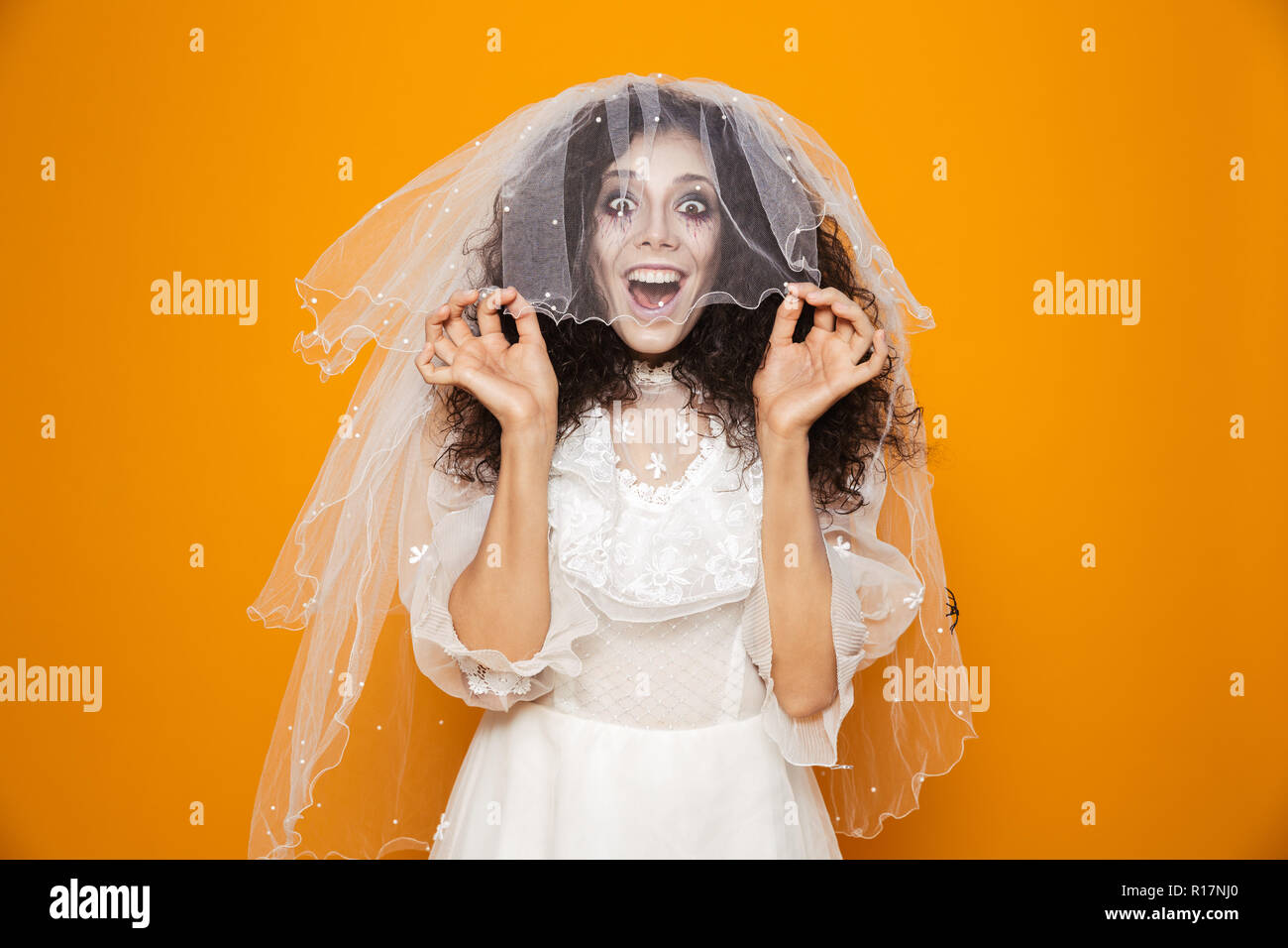 Happy dead bride in wedding dress put on veil and smiling to camera ...
