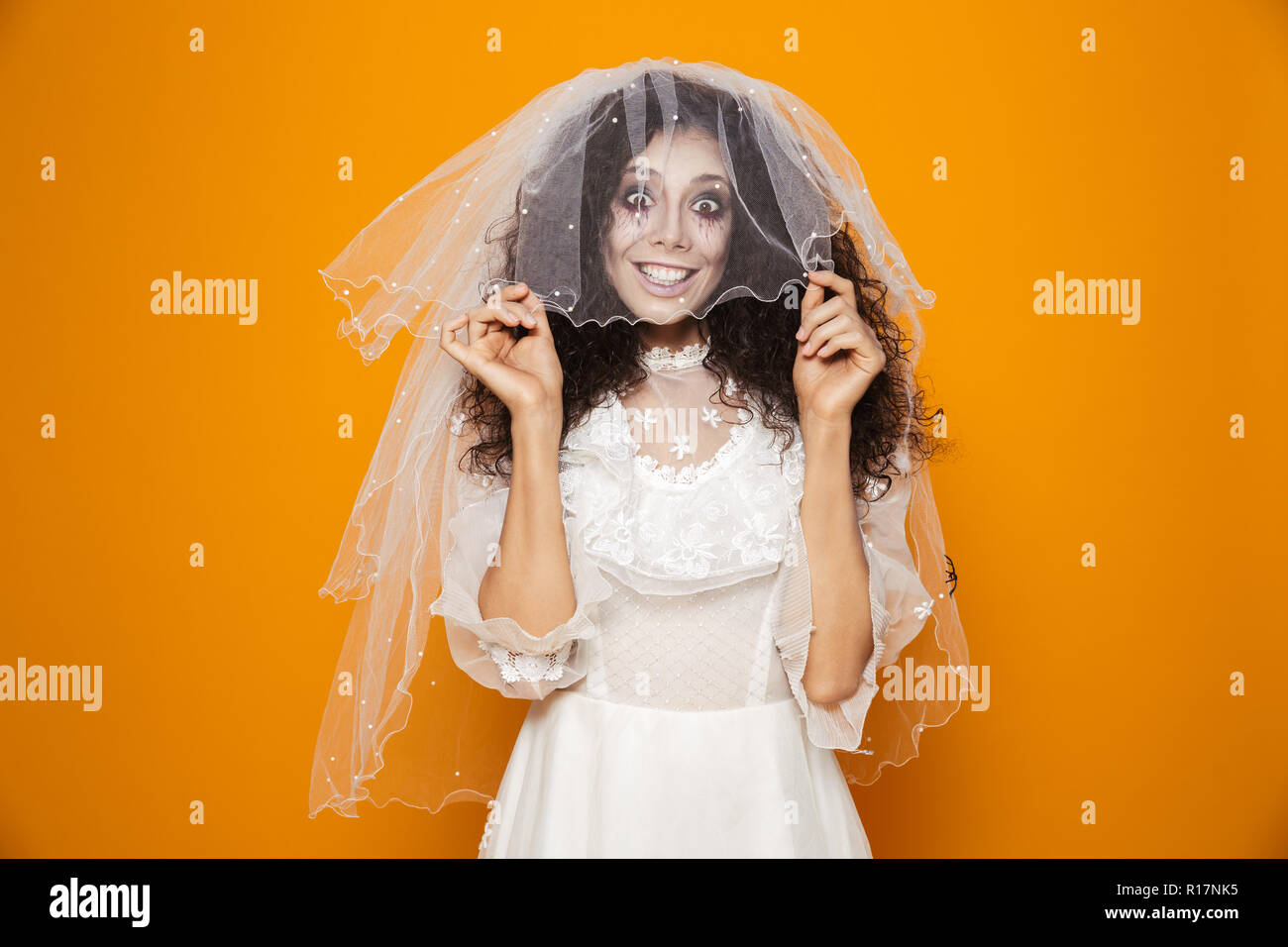 Happy dead bride in wedding dress put on veil and smiling to camera ...