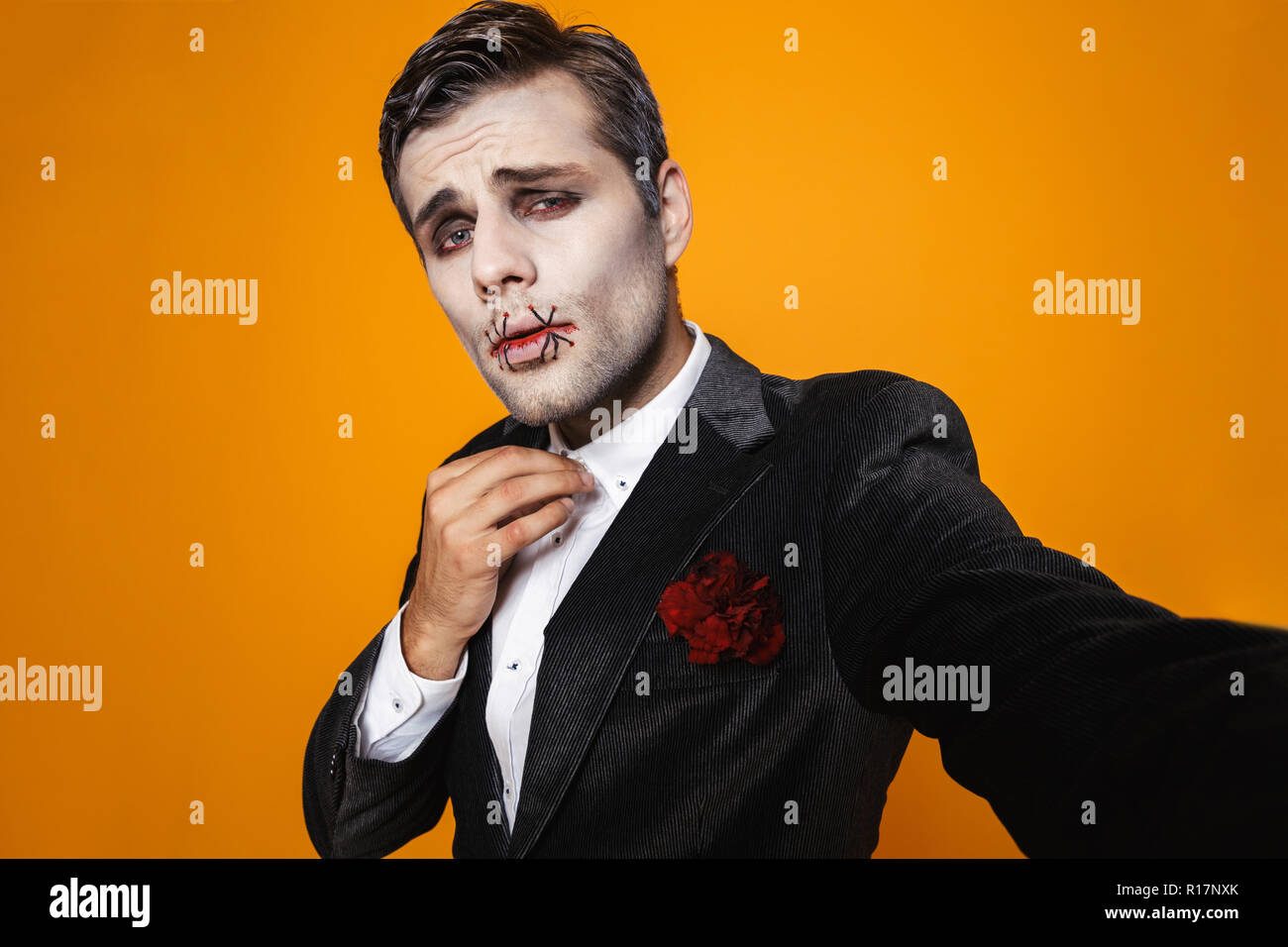 Handsome zombie man with halloween make-up and in suit making selfie ...