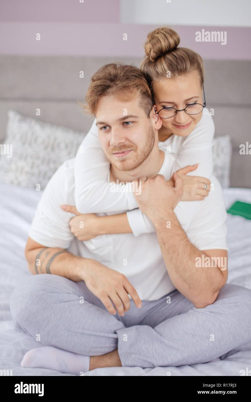 good looking couple embraces passionately, sits on comfortable bed ...