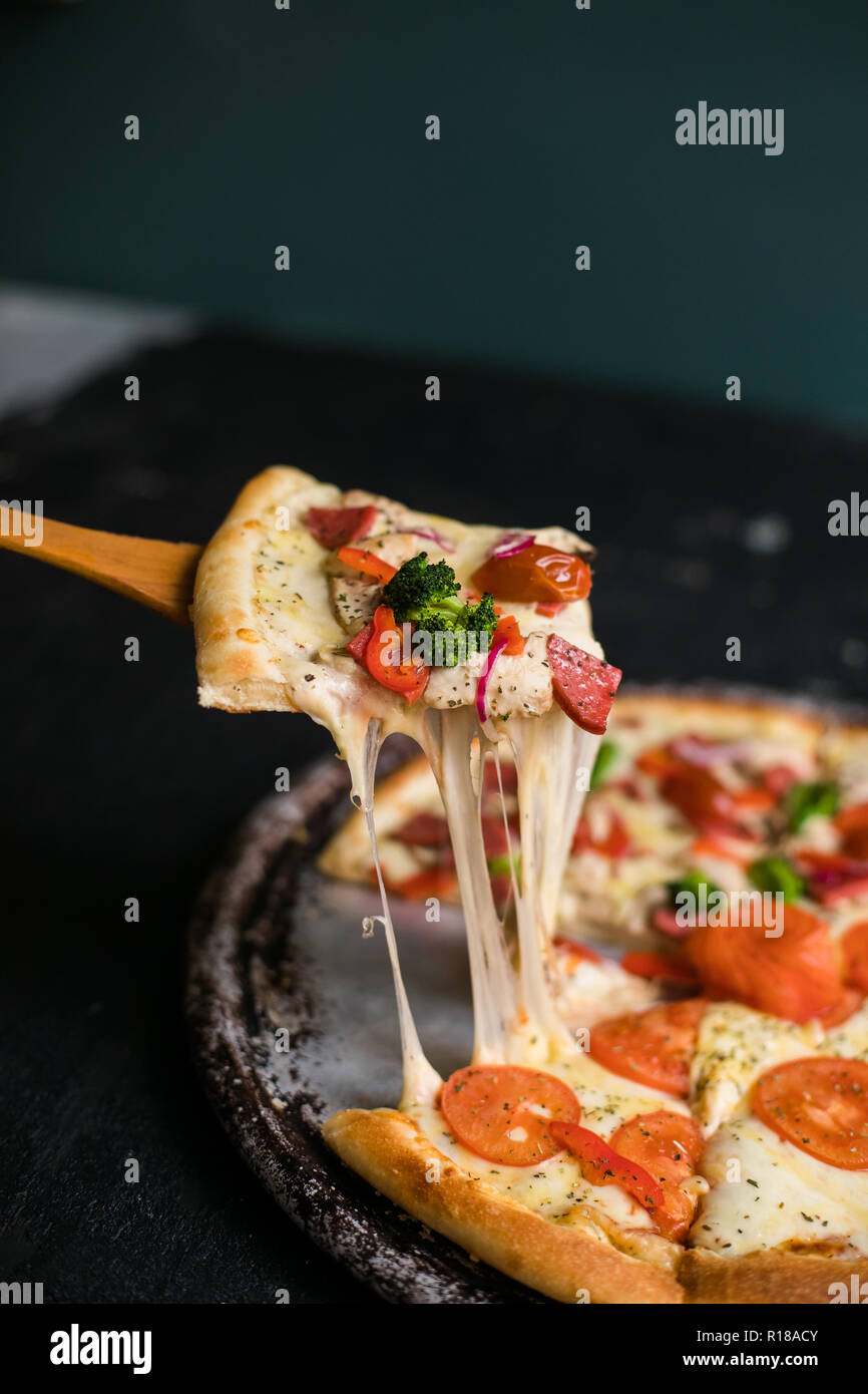 Delicious cheese stringy slice lifted of full supreme pizza baked fresh out of the oven next to ...