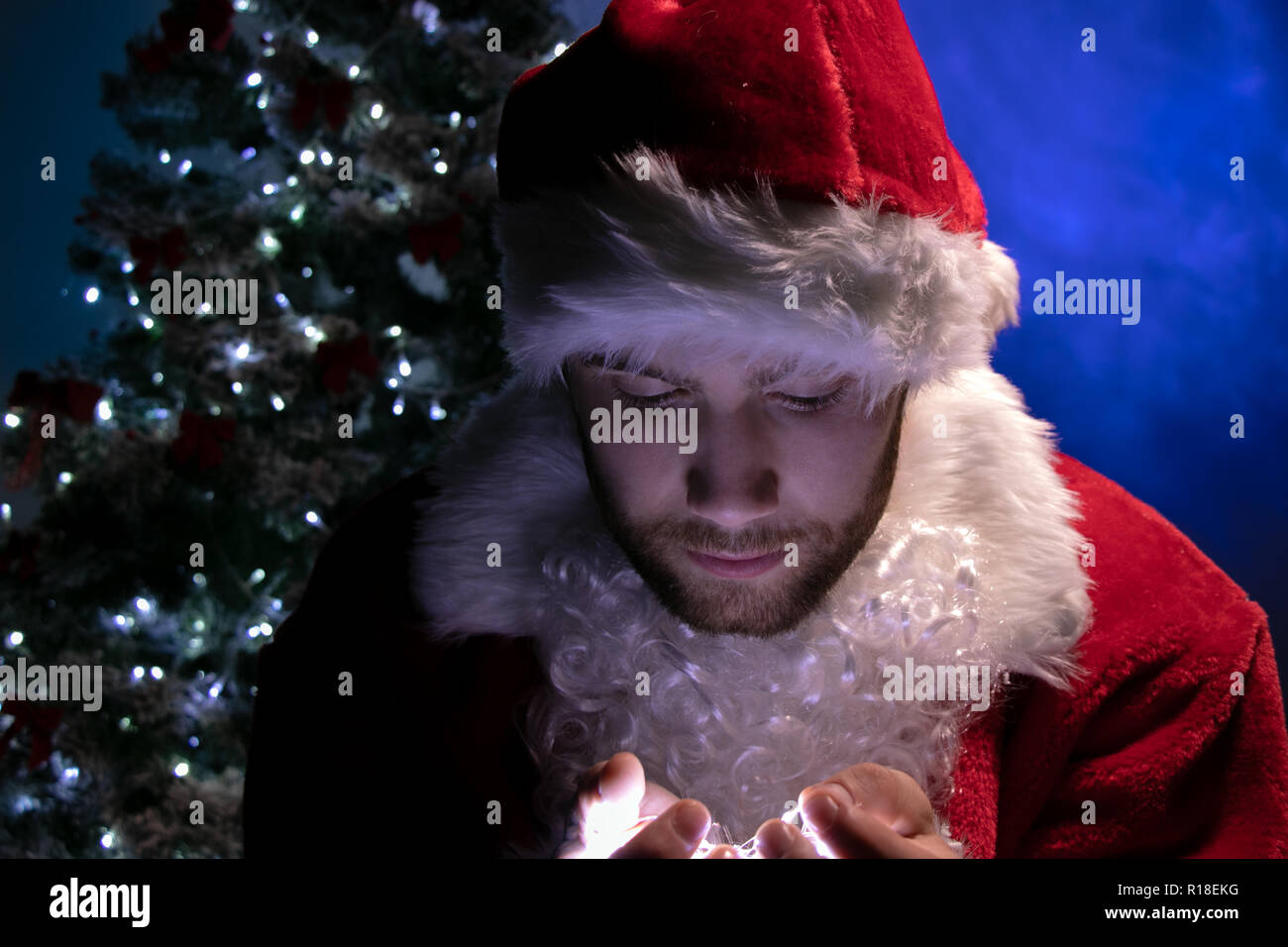 Good looking male santa looking down at lights in his hands in front of ...