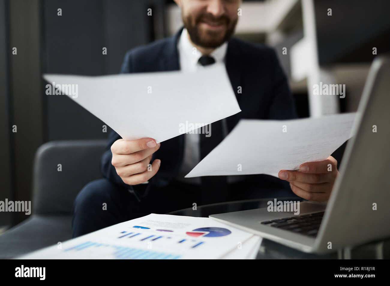 Contemporary businessman looking through contracts or financial papers ...