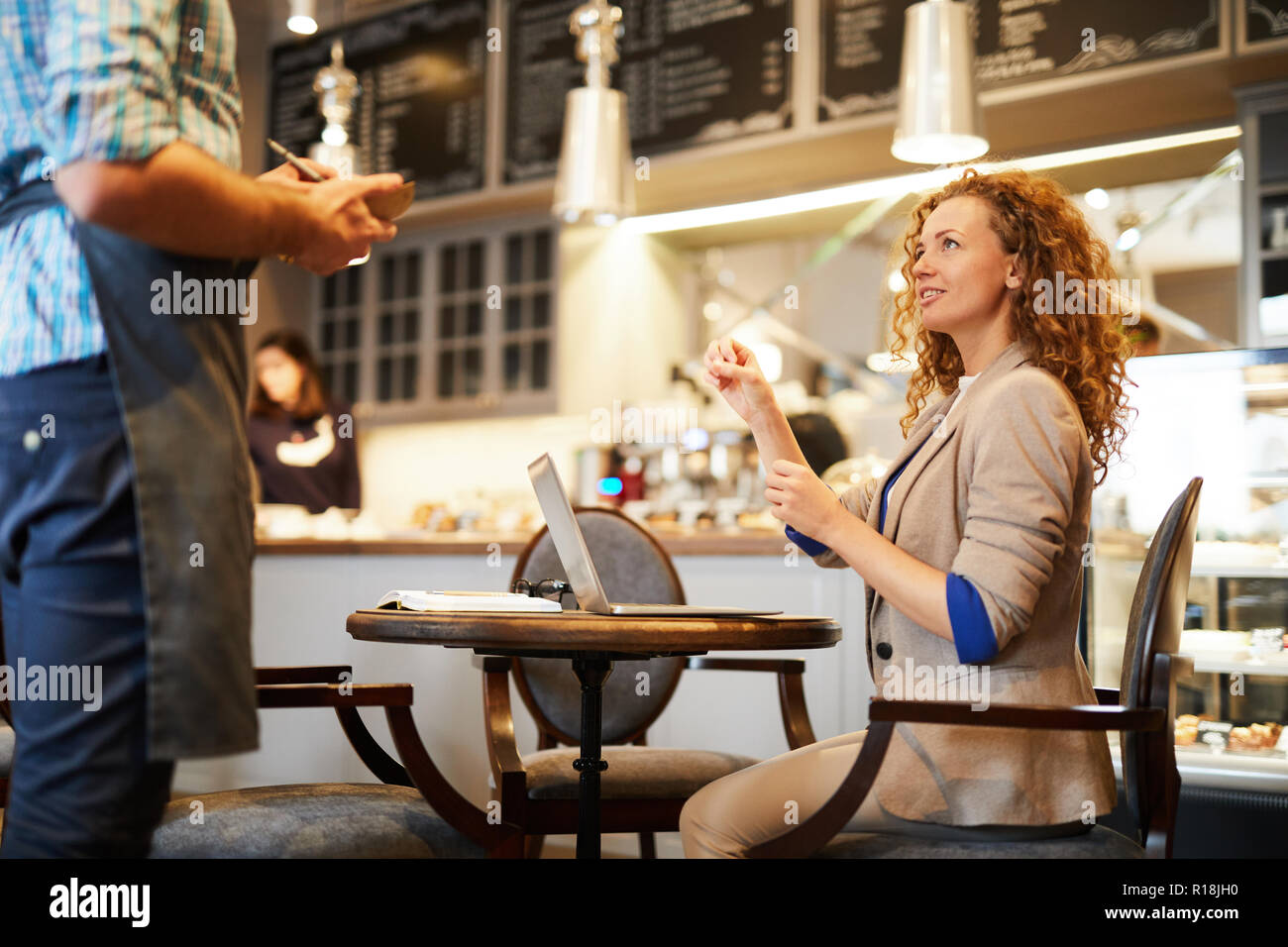 Young woman explaining to waiter which dessert she would like to have ...
