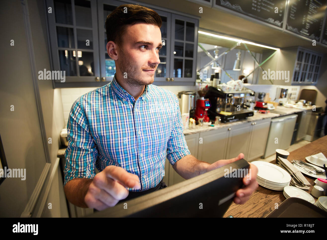 Young sales clerk standing by counter in front of computer and entering ...