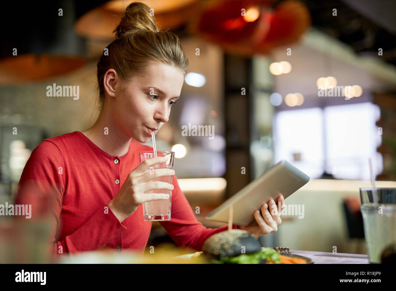 Modern girl sipping soda through straw while watching movie at leisure ...