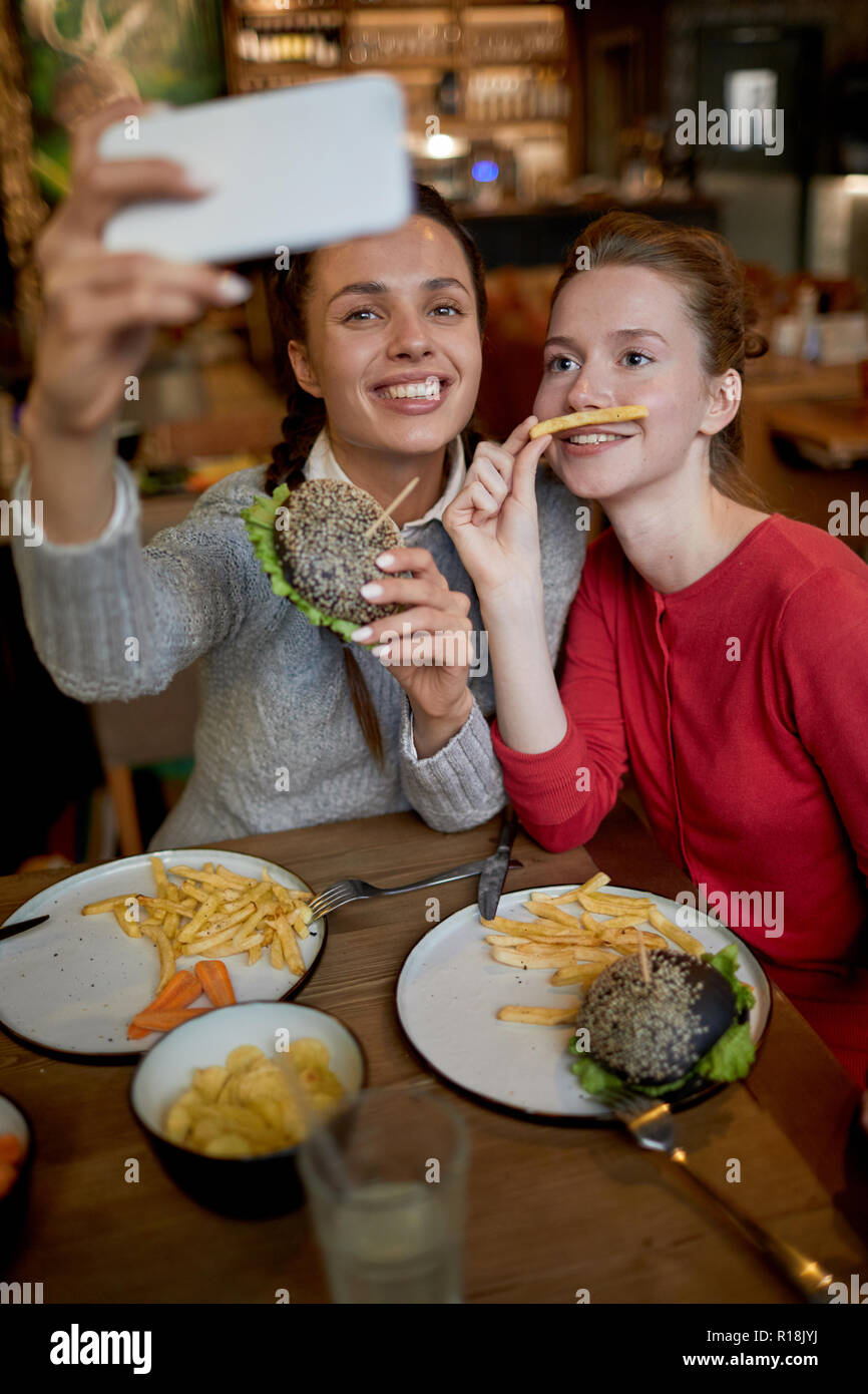 Two friendly girls making funny selfie with fast food while having ...