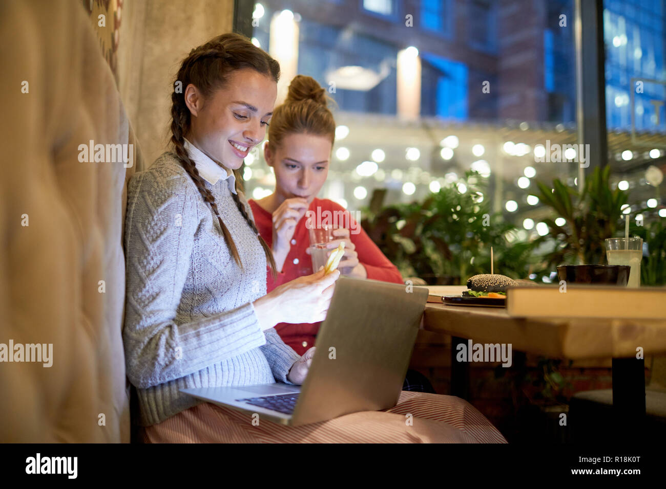 Two casual students with laptop eating fast food and drinking soda ...