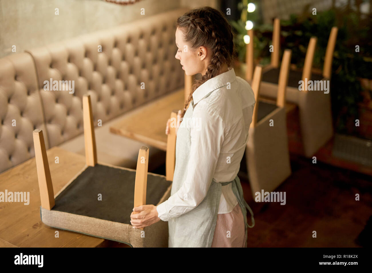 Cafe staff in workwear putting chairs upside down on tables after ...
