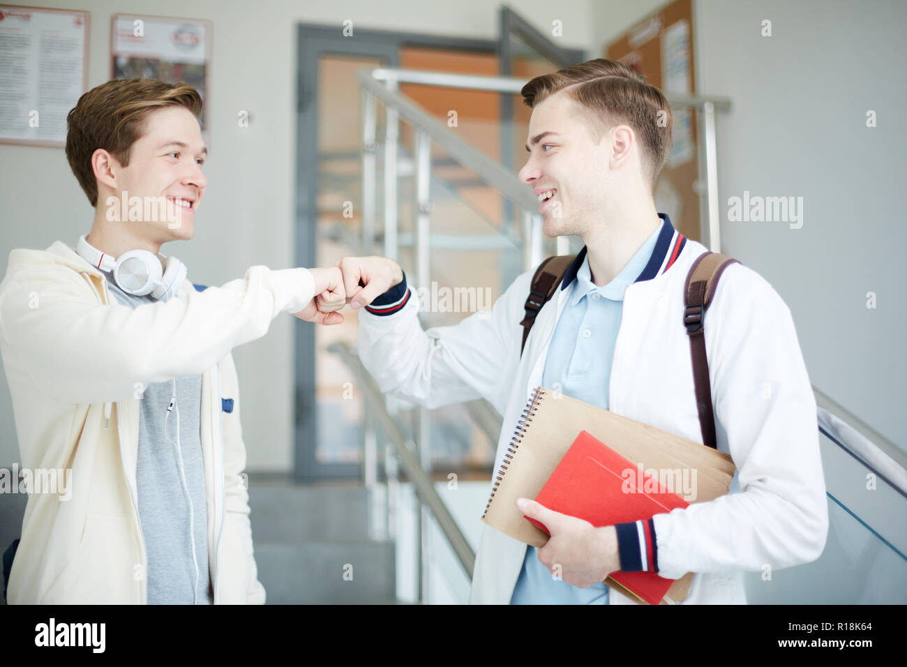 Two happy and successful students in casualwear bumping thair fists ...