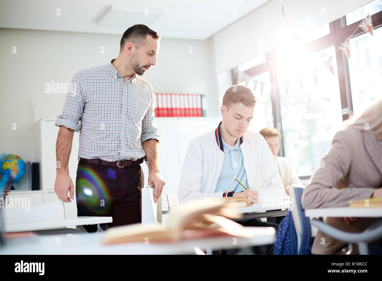 Serious teacher looking at one of students notes during individual work ...