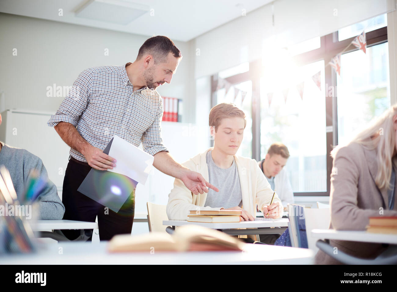 Strict teacher pointing at notes of one of students at lesson during ...