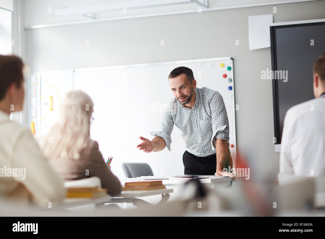 Confident teacher commenting one of students answer while explaining ...