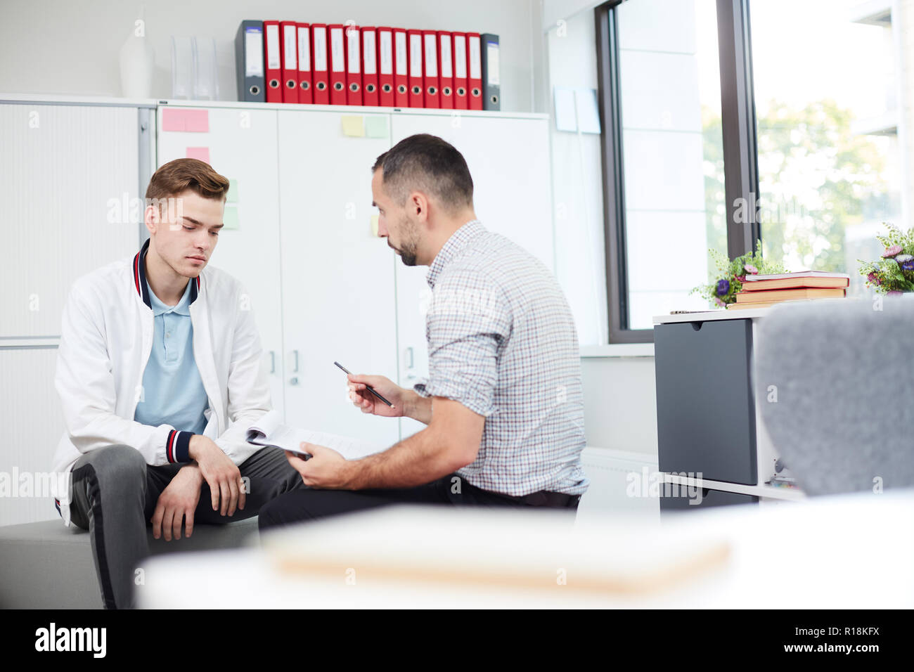 Sad student listening to teacher advice and commenting on his paper at ...