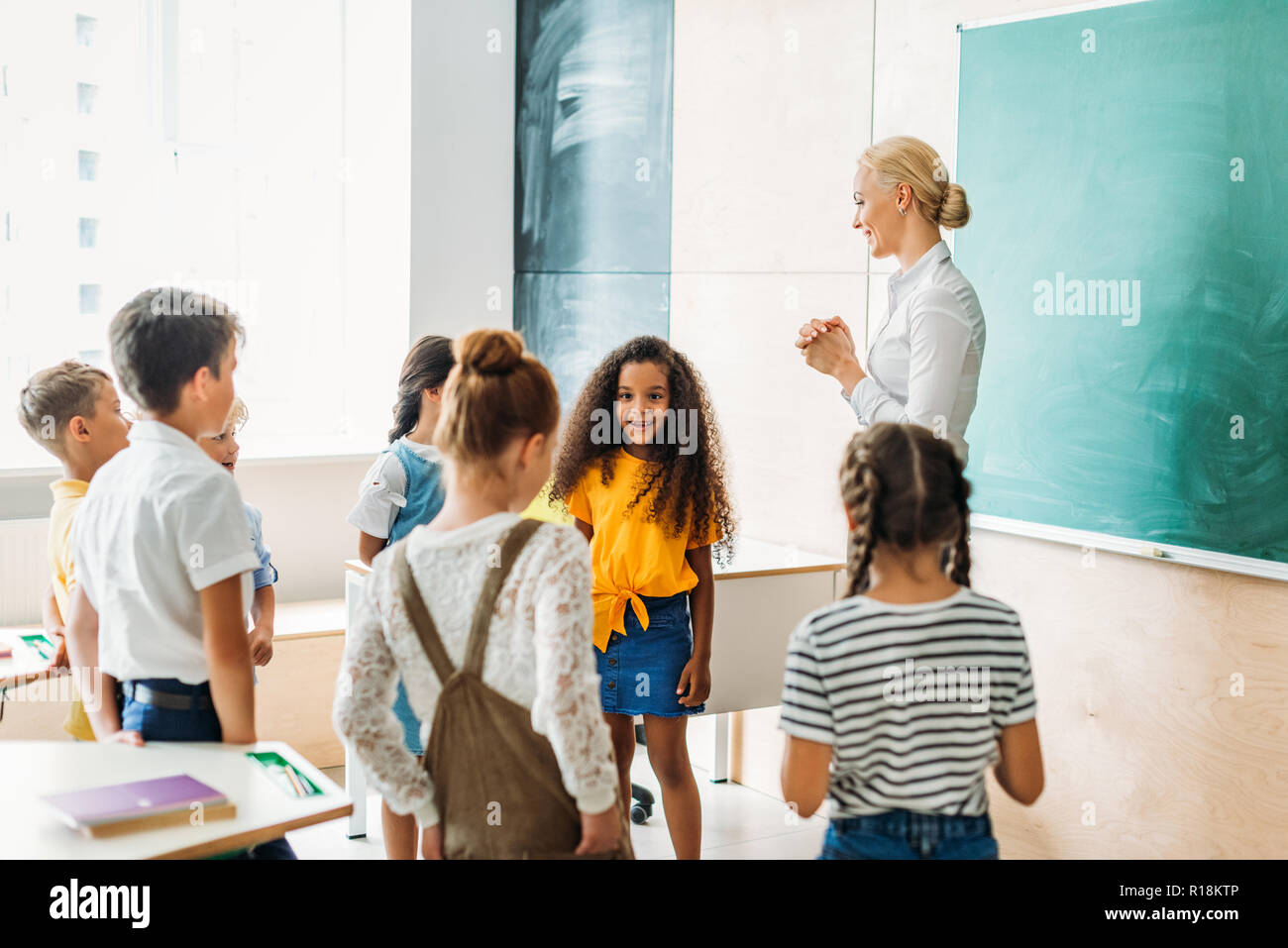 happy multiethnic classmates standing around teacher at classroom Stock ...
