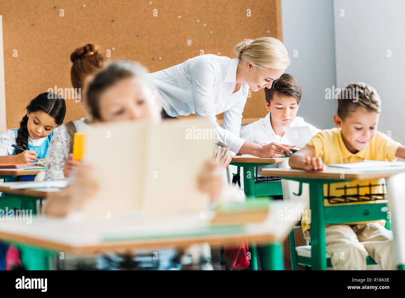 smiling teacher helping children with work during lesson Stock Photo ...