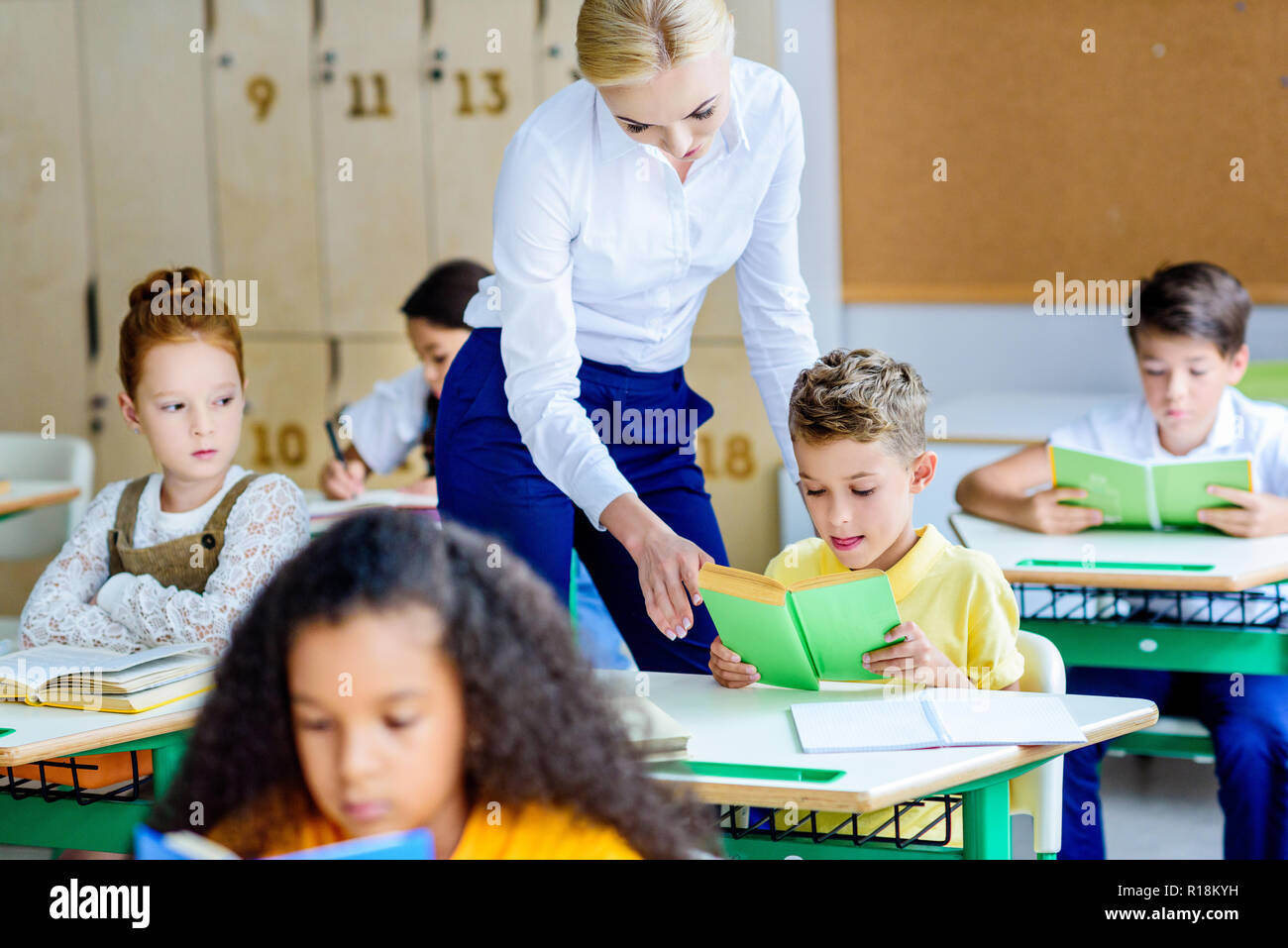 beautiful teacher checking how kids reading books during lesson Stock ...