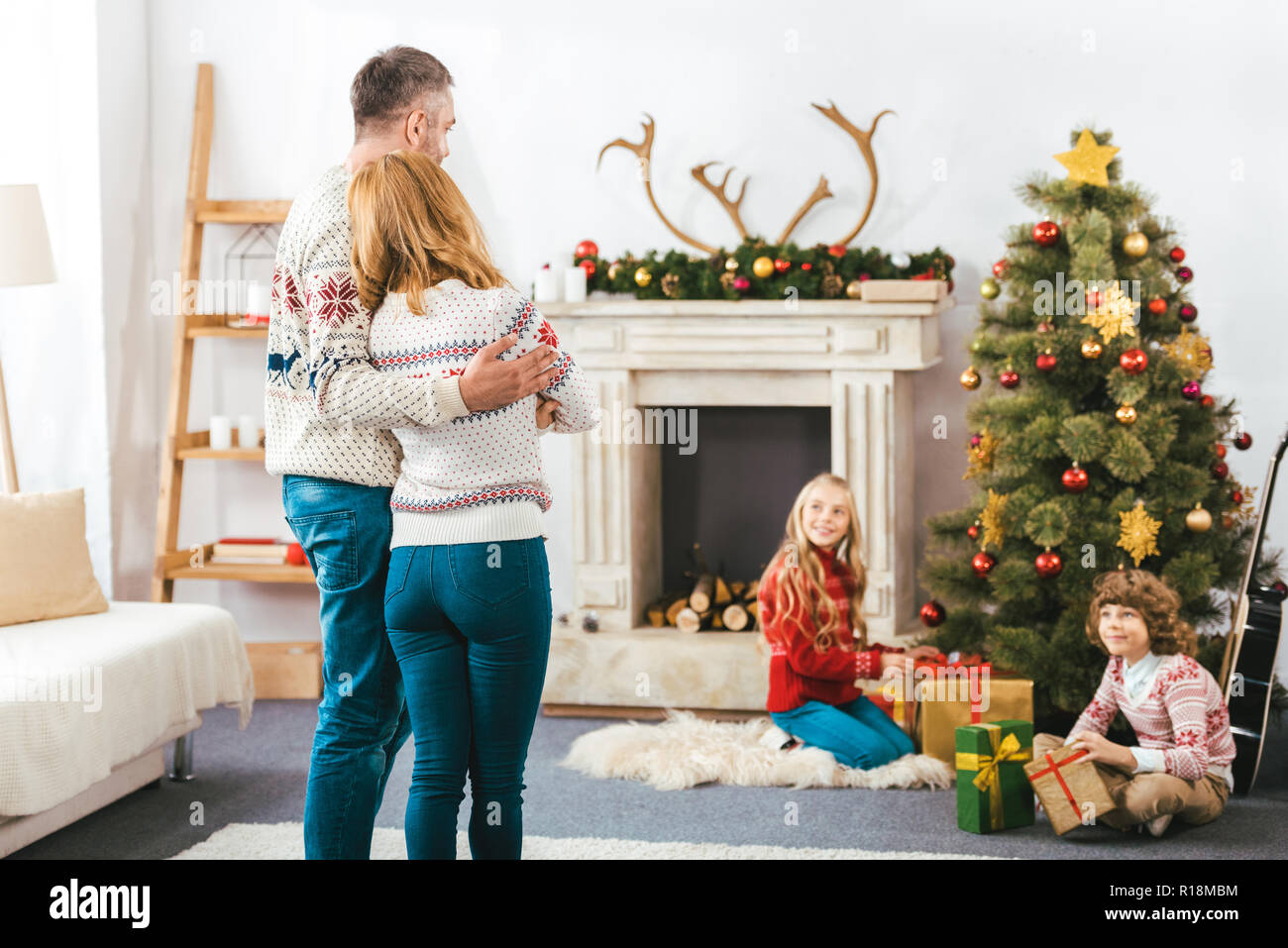 happy parents embracing and looking at kids opening gift boxes on ...
