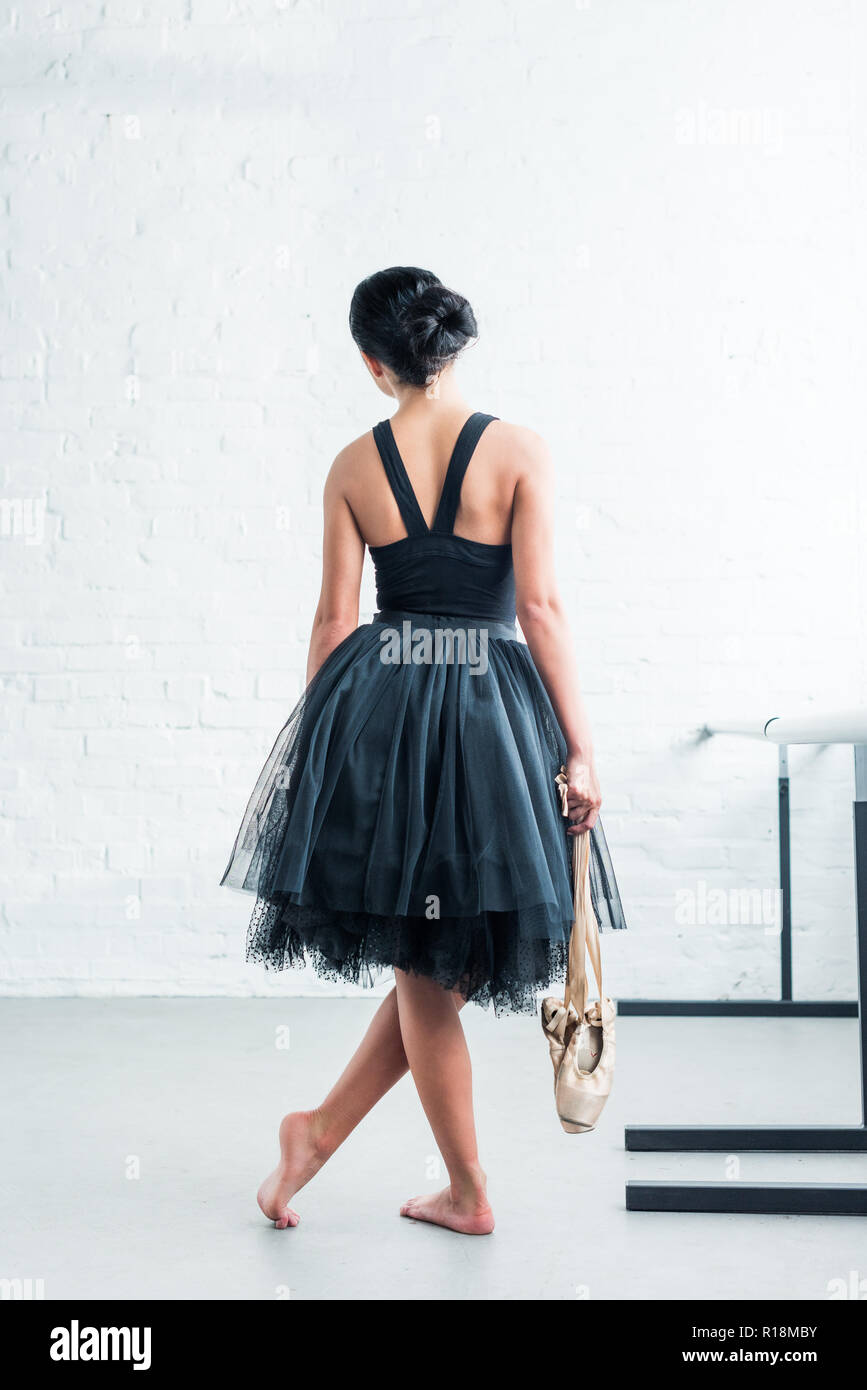 back view of young ballerina holding pointe shoes while standing in ...