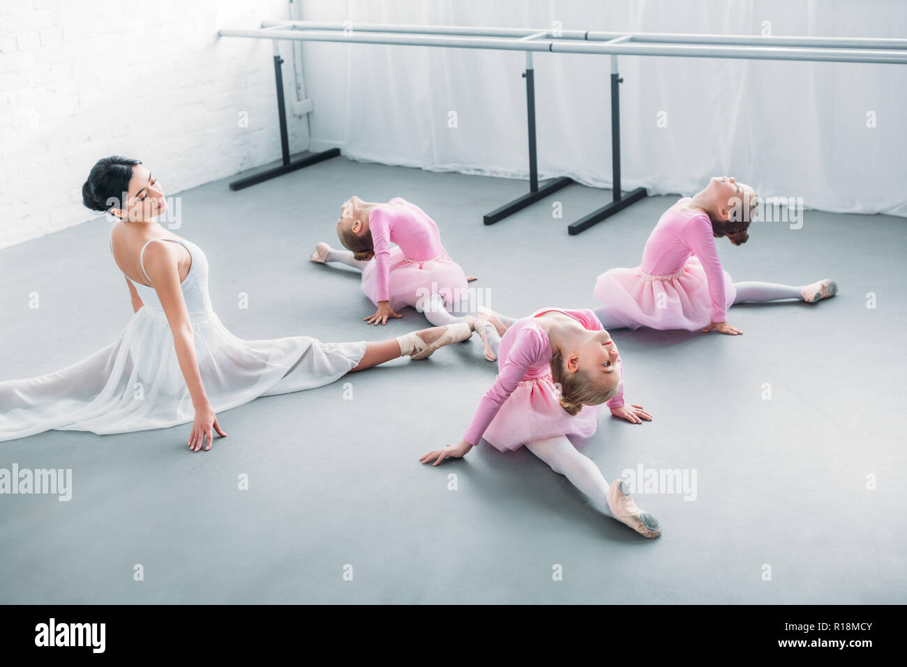 adorable little ballerinas and young teacher stretching and exercising ...