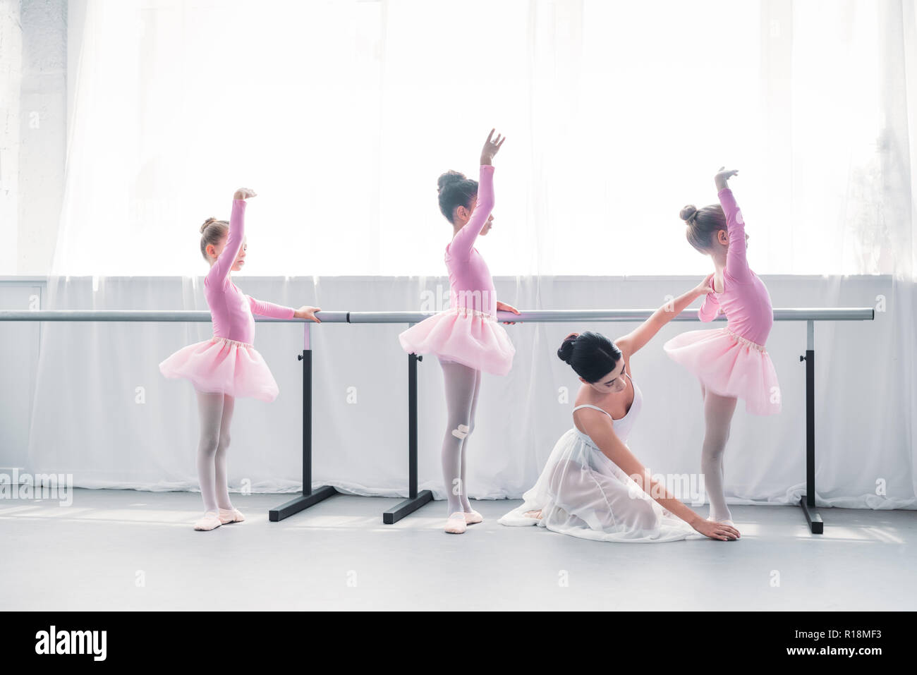 side view of young ballet teacher exercising with kids in ballet school ...