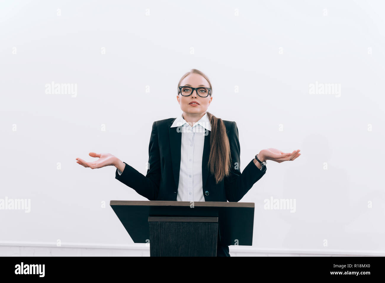 attractive lecturer standing at podium tribune and showing shrug ...