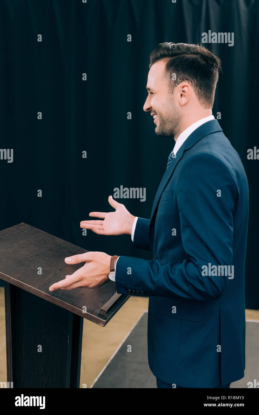 side view of handsome lecturer standing and gesturing at podium tribune ...