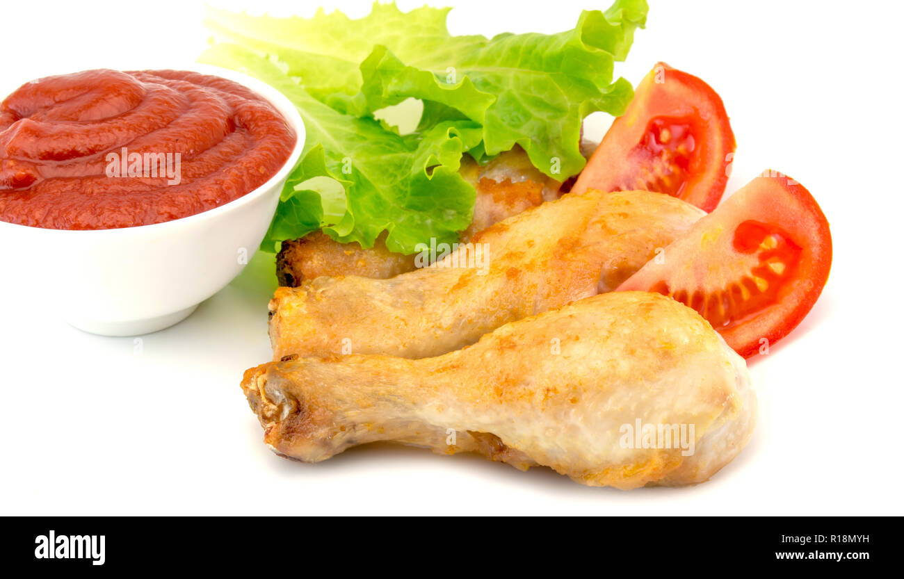 chicken legs on a white plate with slices of tomato and lettuce and ...