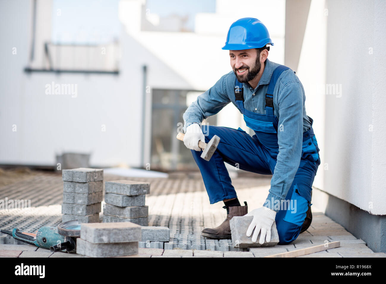 Builder in uniform laying paving tiles on the construction site with ...