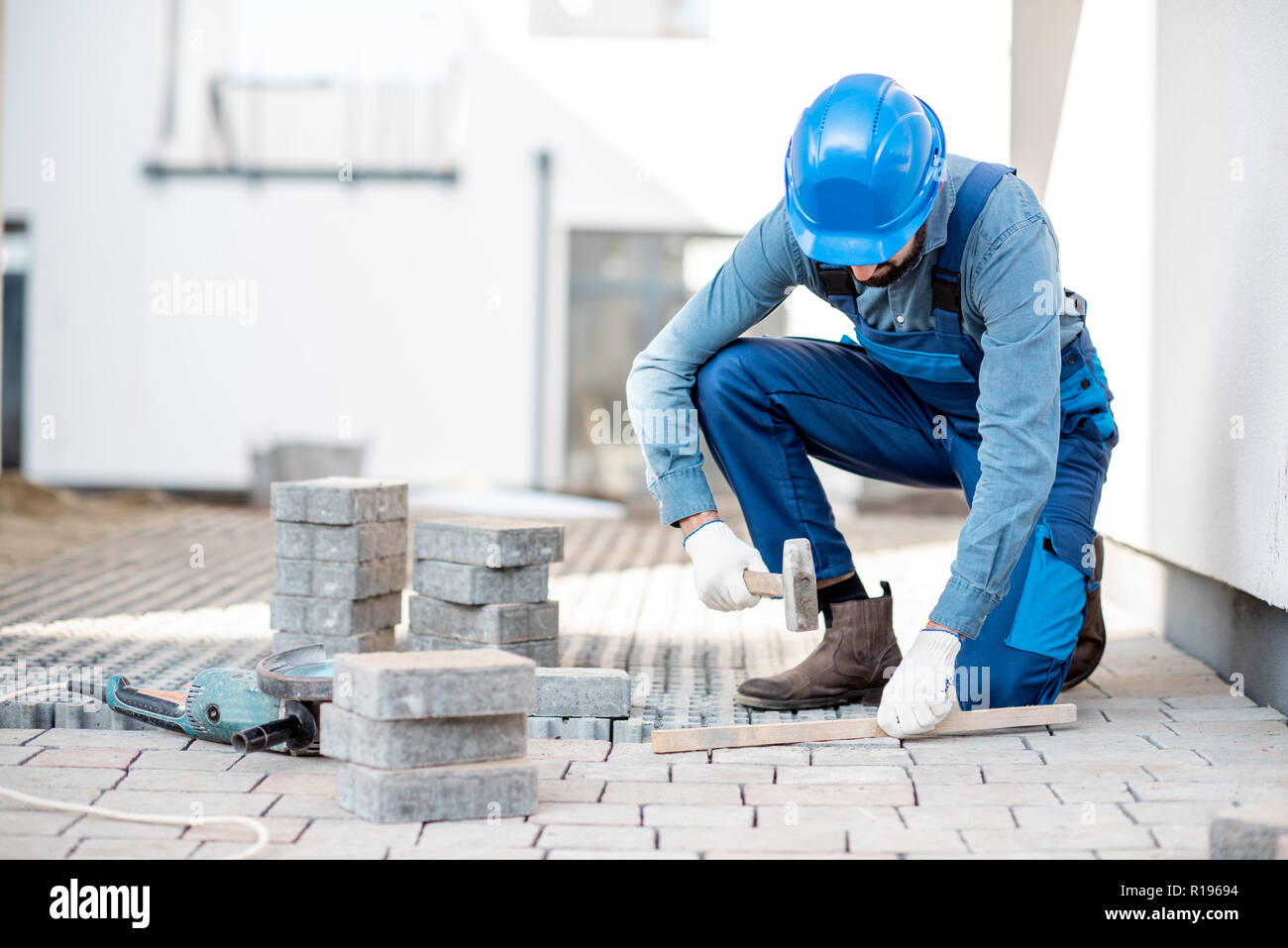 Builder in uniform laying paving tiles on the construction site with ...