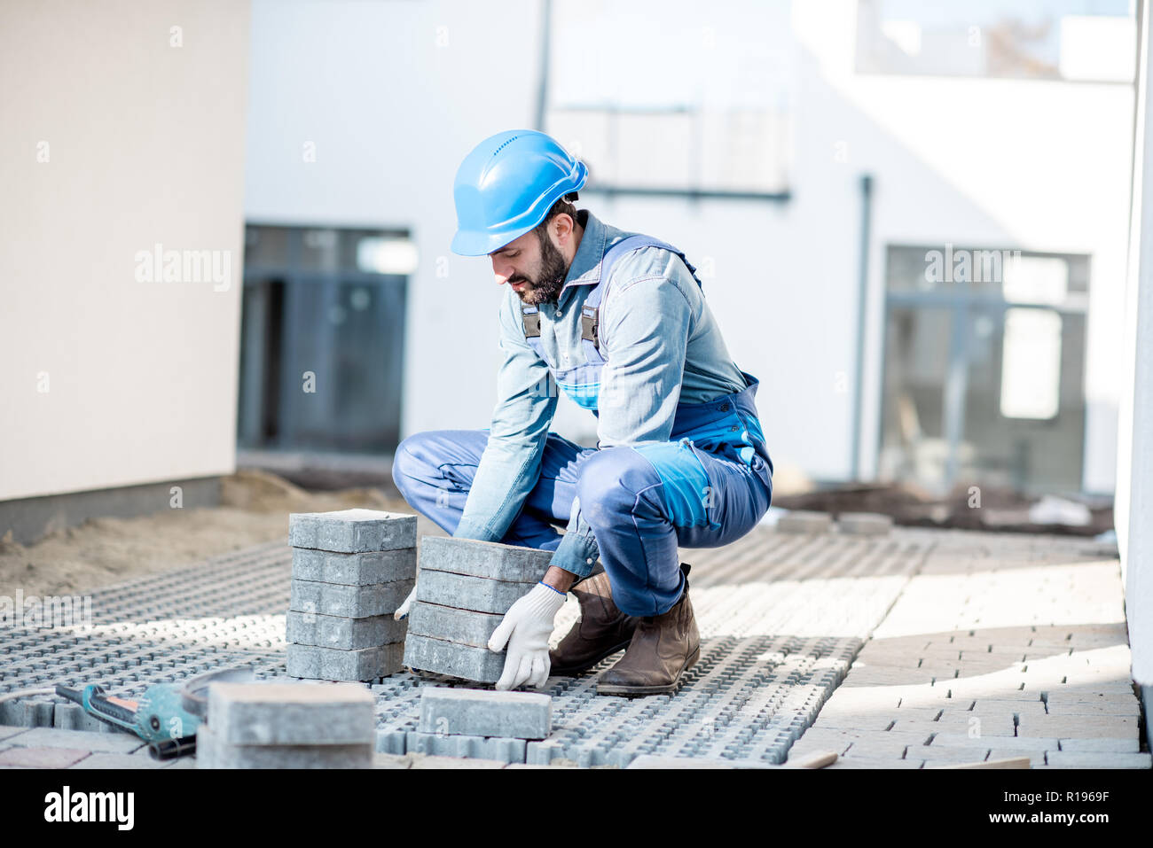Builder in uniform laying paving tiles on the construction site with ...