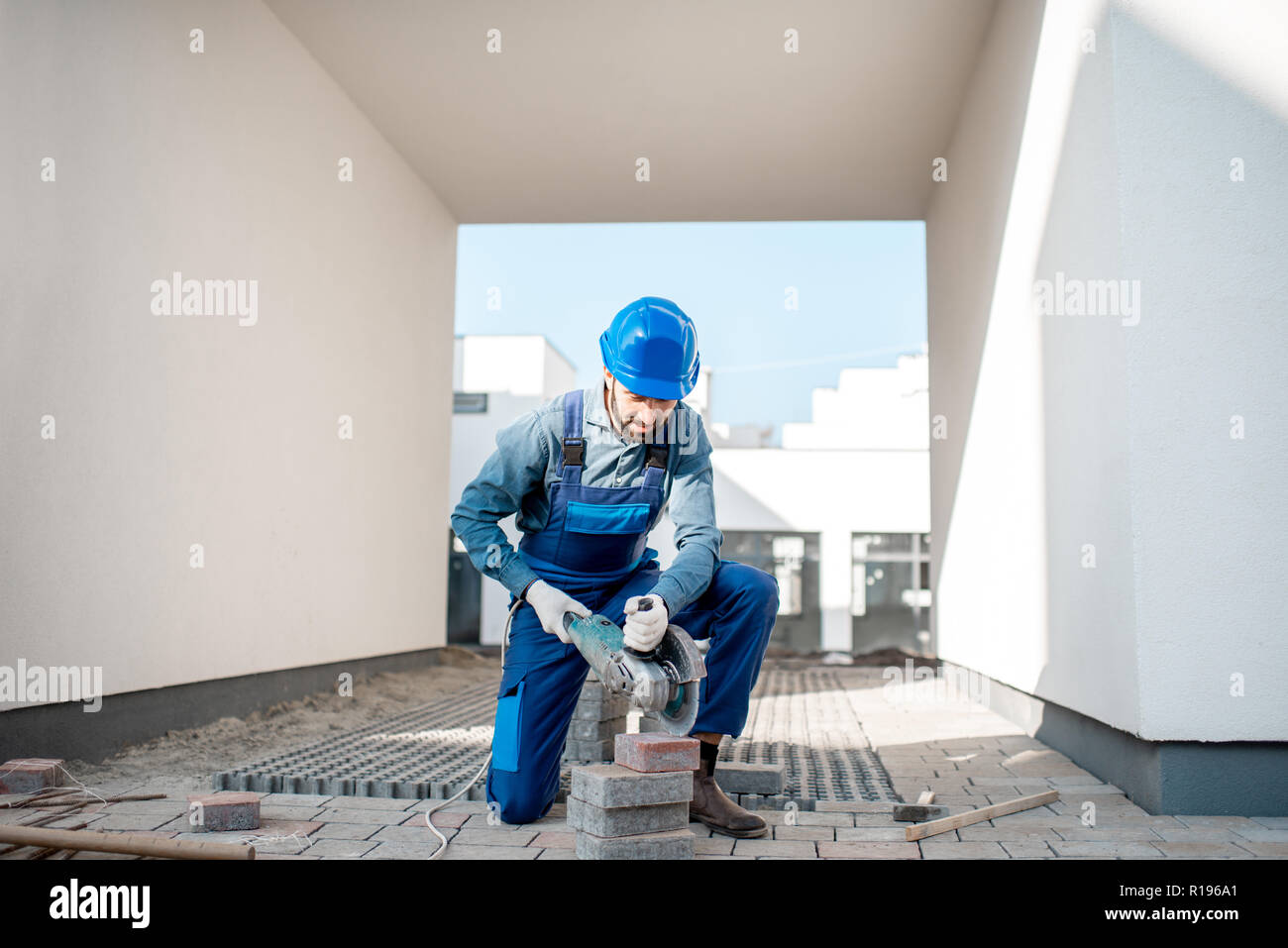 Builder in uniform cutting paving tiles with electric cutter on the ...
