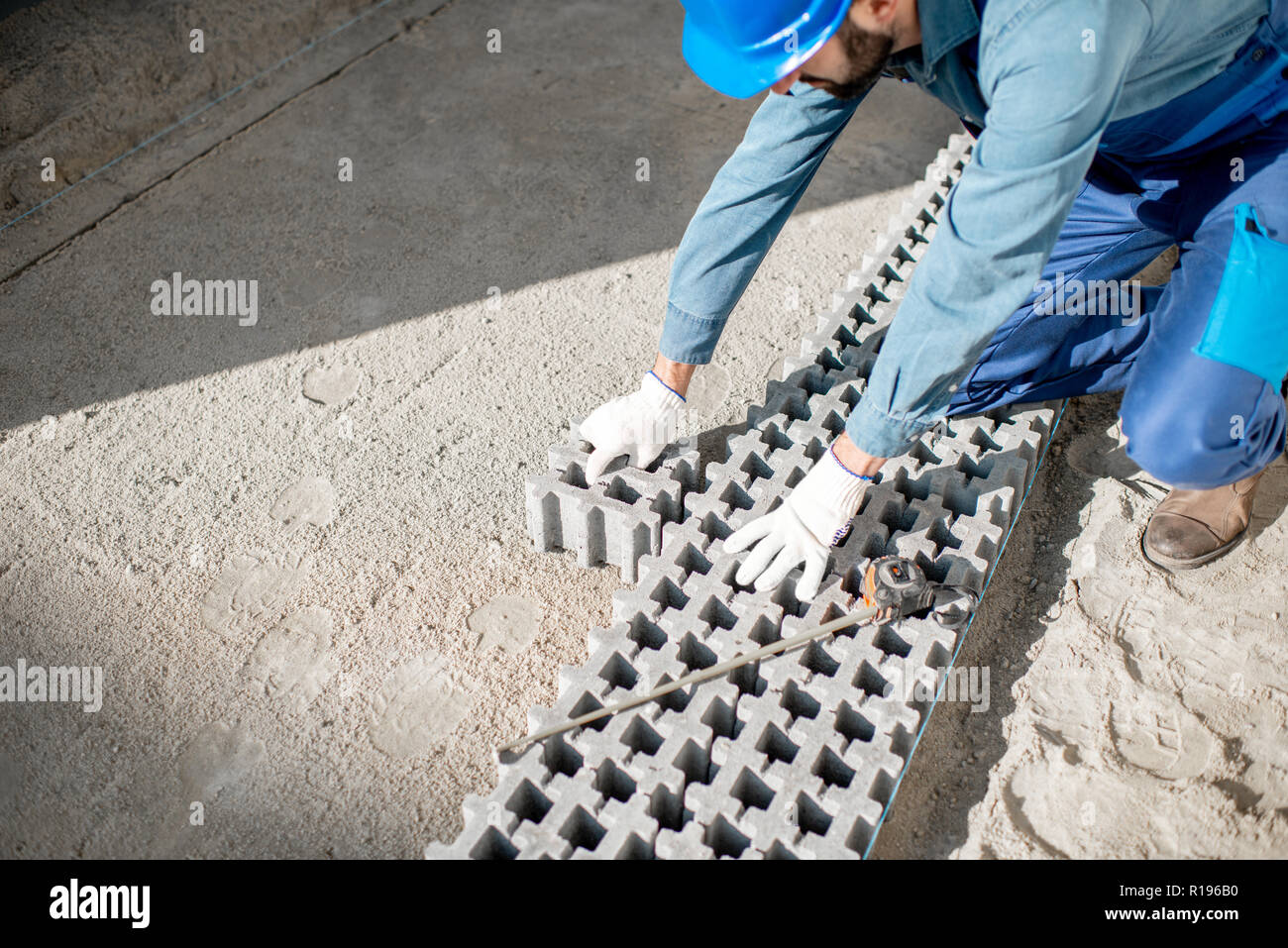 Builder laying paving tiles with holes for grass on the construction ...