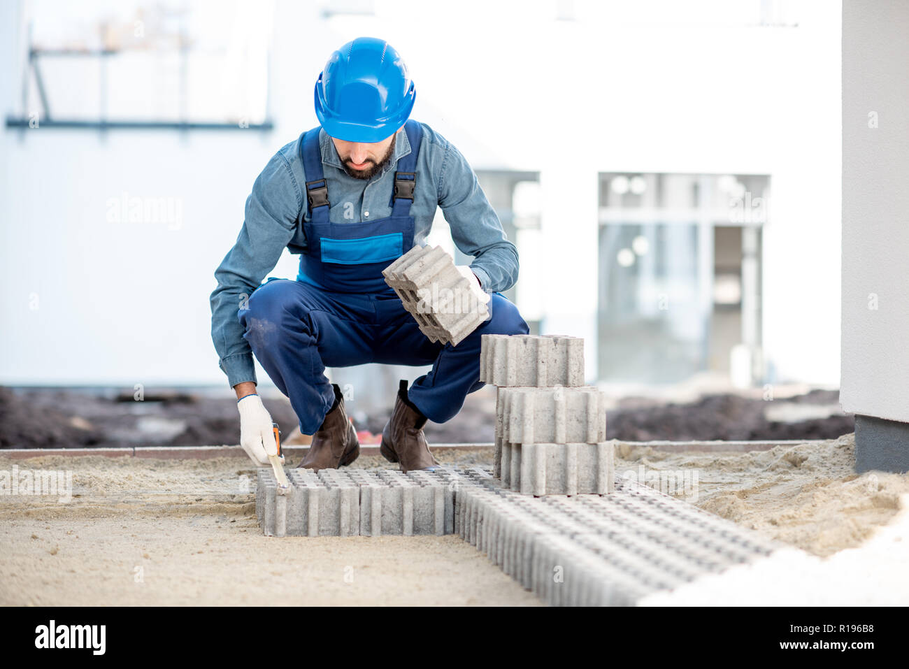 Builder in uniform laying paving tiles on the construction site with ...